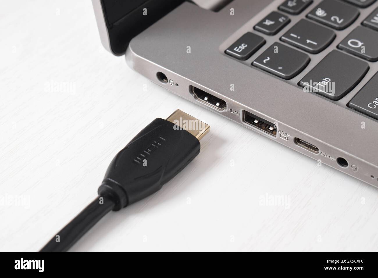 Man is connecting black HDMI cable into HDMI port of the modern laptop ...