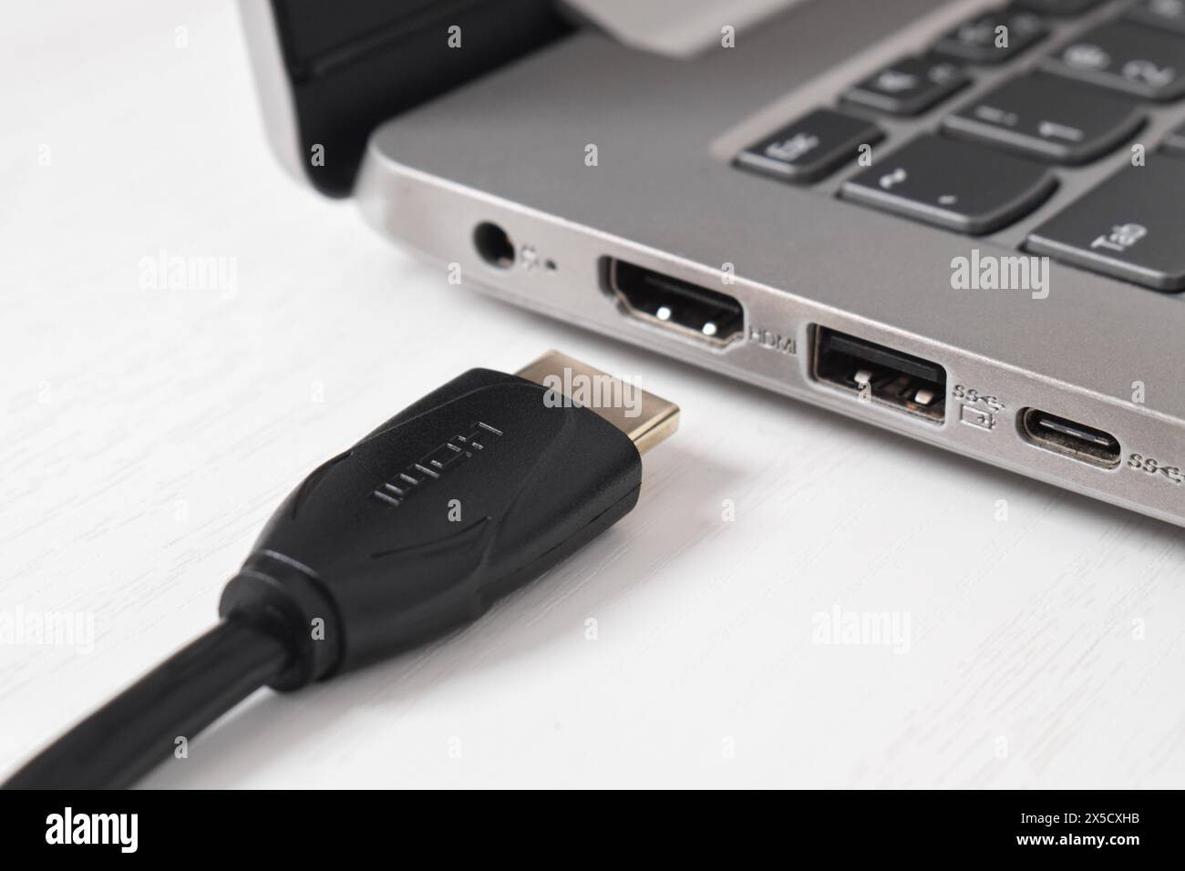 Man is connecting black HDMI cable into HDMI port of the modern laptop ...