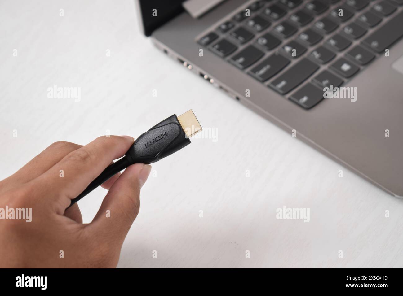 Man is connecting black HDMI cable into HDMI port of the modern laptop ...