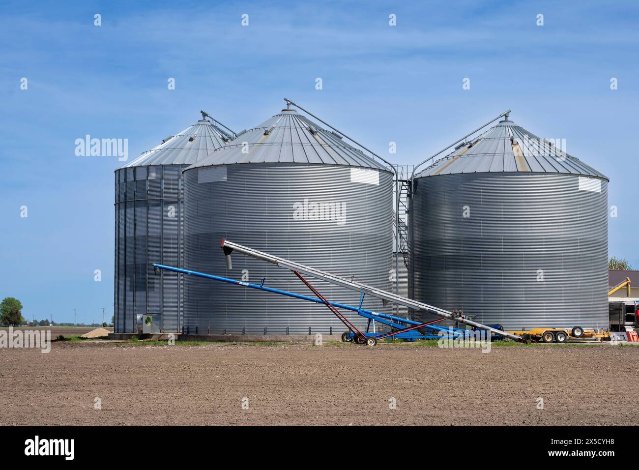 Two large metal grain silos in a field with a conveyor system, under a ...