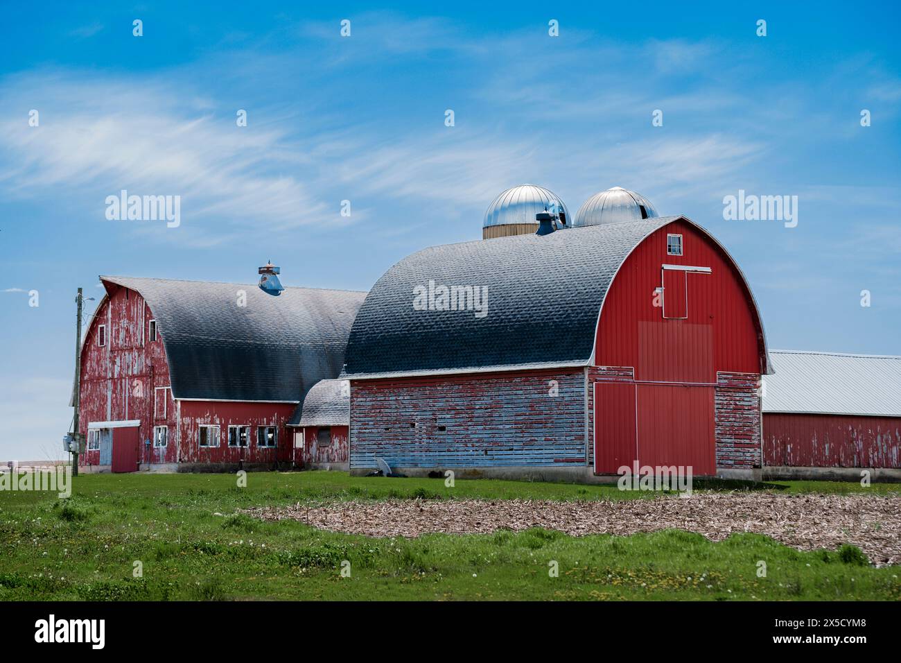 Traditional red barn and a large silver-roofed barn under a blue sky ...
