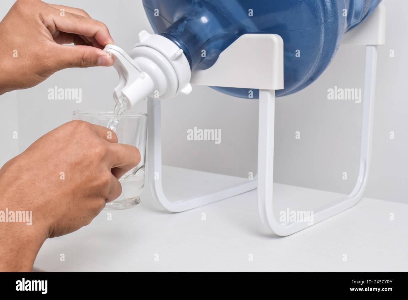 Man's hand pours water into a glass cup from a large gallon. Pouring ...