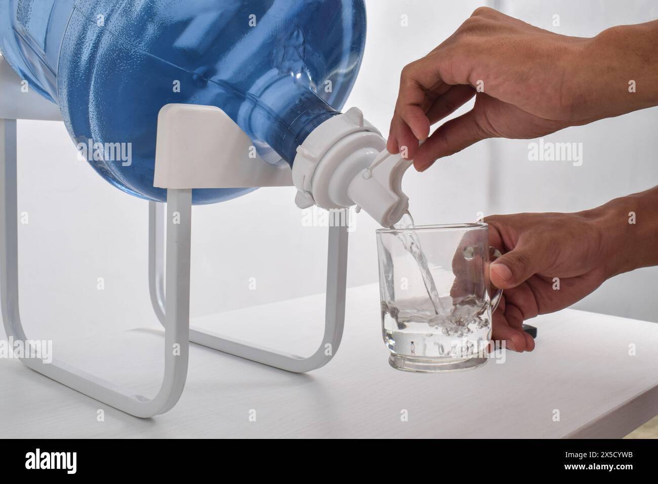 Man's hand pours water into a glass cup from a large gallon. Pouring ...