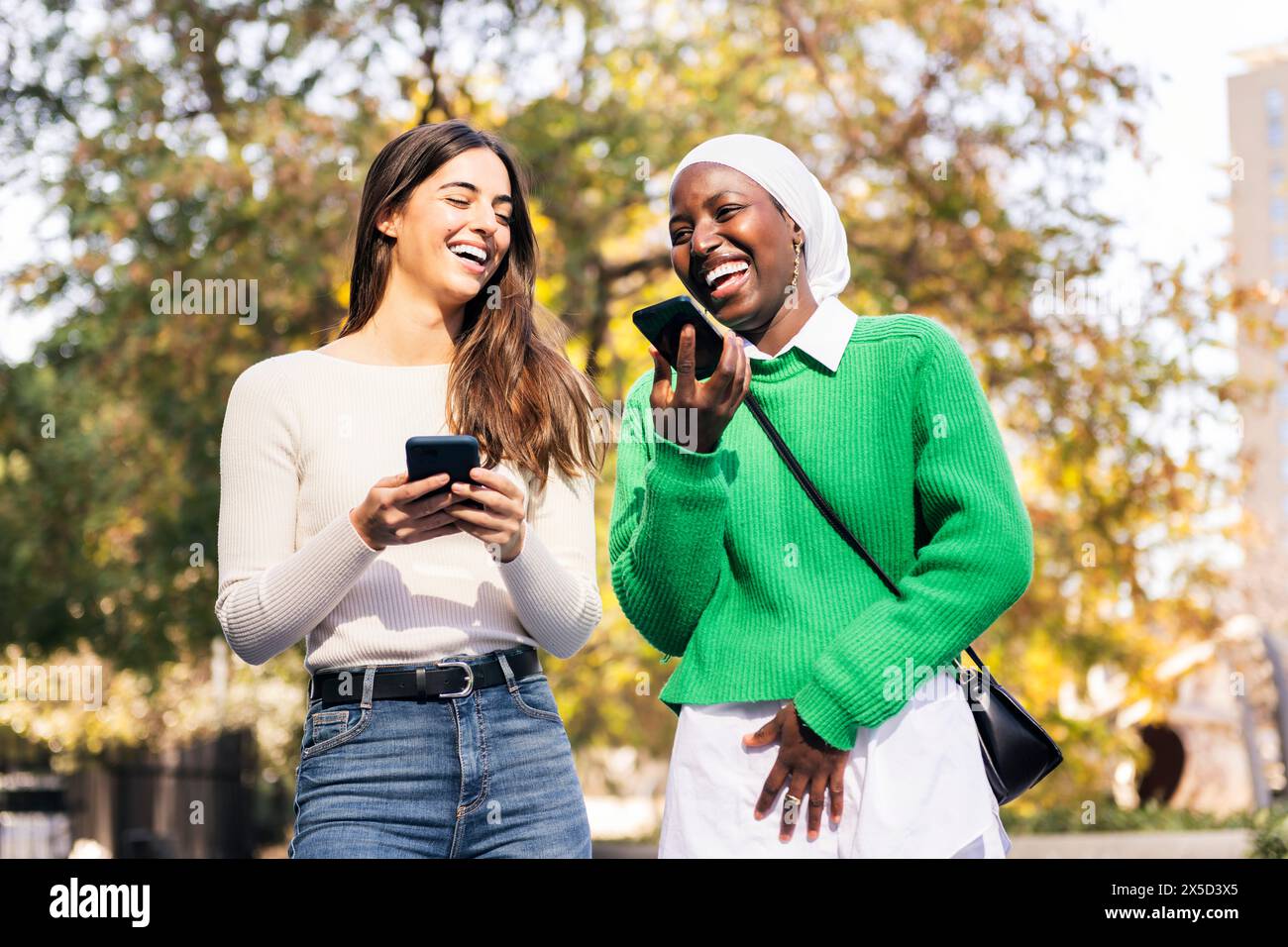 female friends laughing using their mobile phones Stock Photo - Alamy