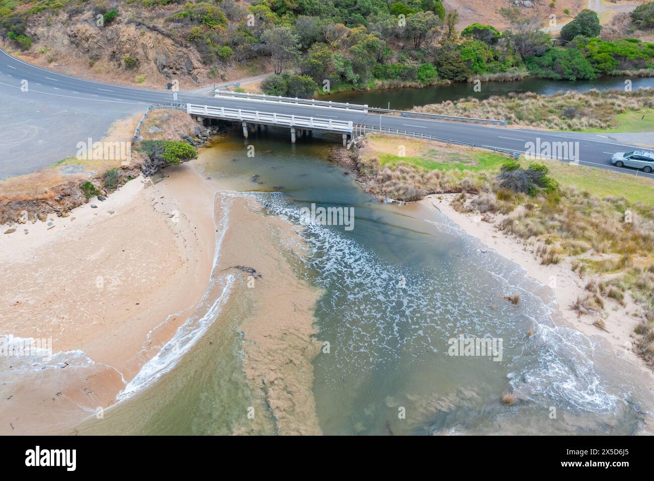 Aerial view of a wave rolling up a coastal river mouth and under a ...