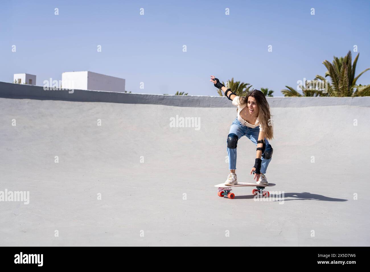 A beginner young woman confidently surfskating down the side of a ramp ...