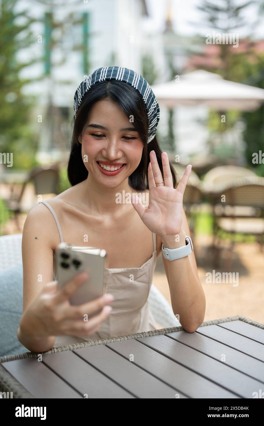 An attractive Asian woman in a cute dress waves her hand, greeting ...