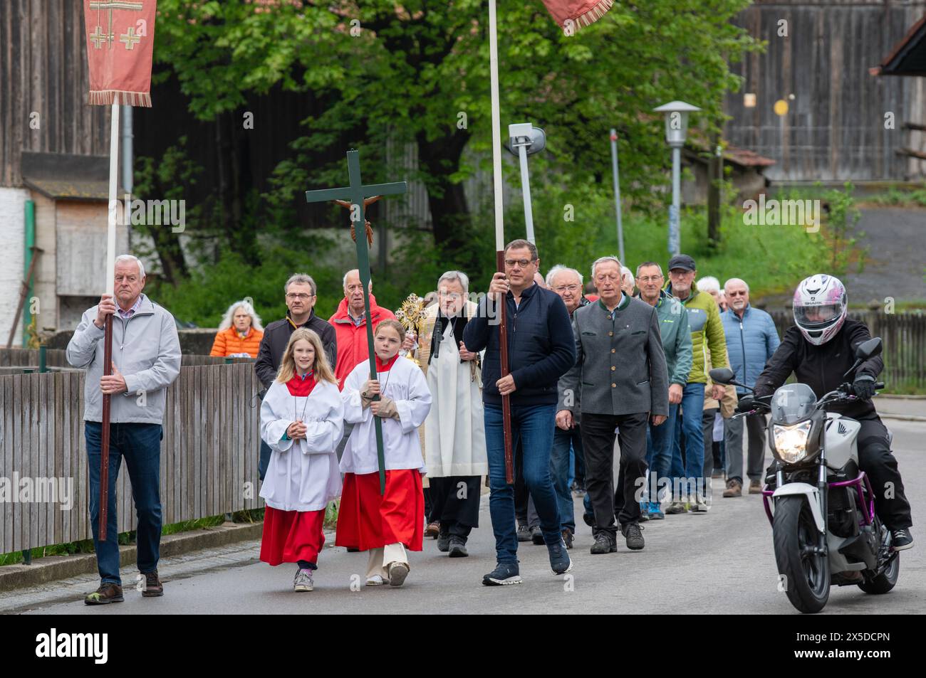 09 May 2024, Bavaria, Roßhaupten: A motorcyclist passes parishioners on ...