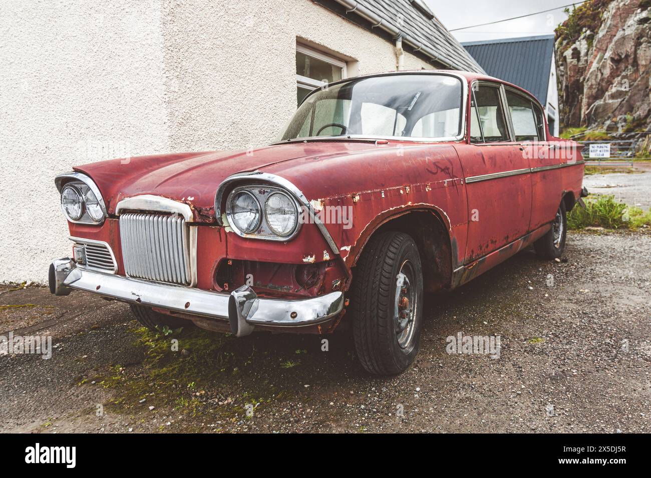 Old maroon car abandoned next to a house. Its bodywork reflects the ...