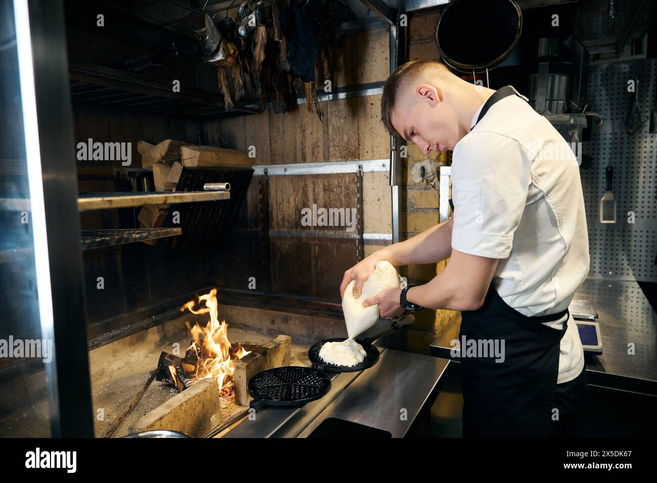 Side of chef pouring dough on pancake maker at burning fire place in ...