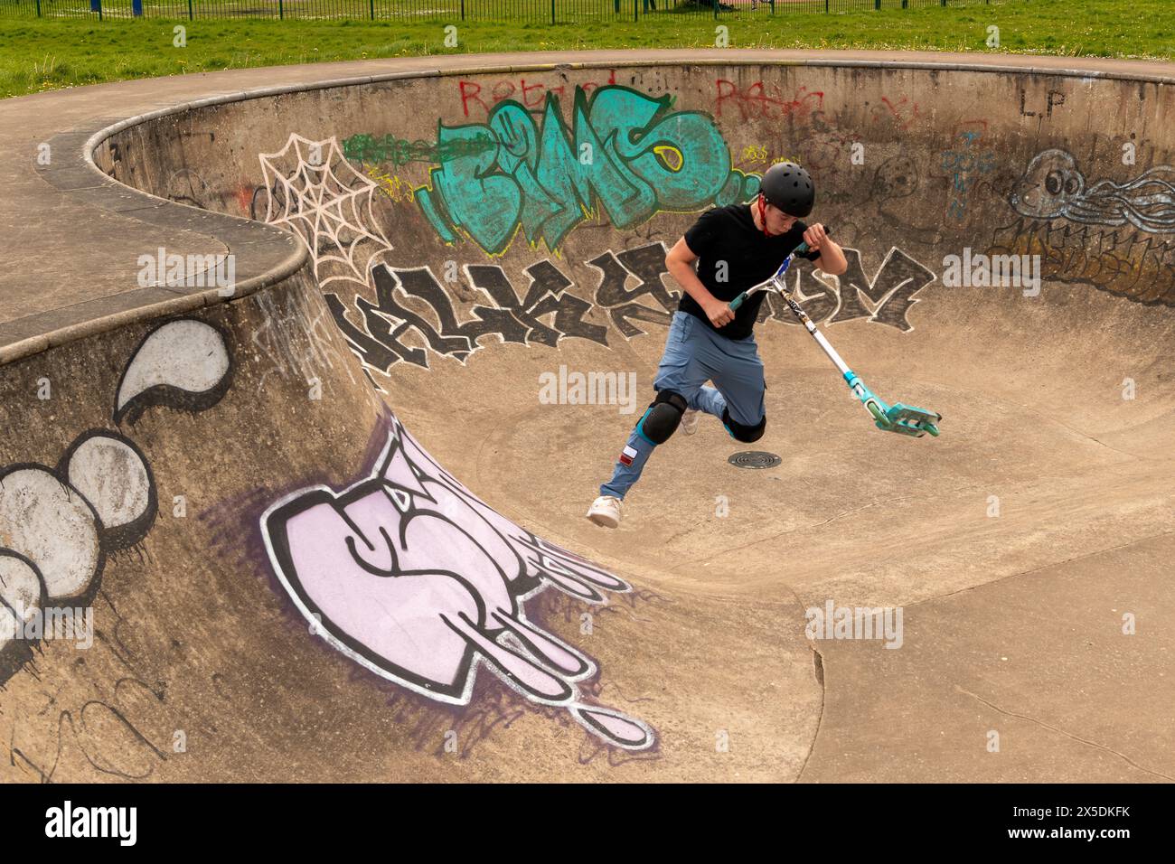 Youth in a black shirt does spinning stunts on a stunt scooter at the ...