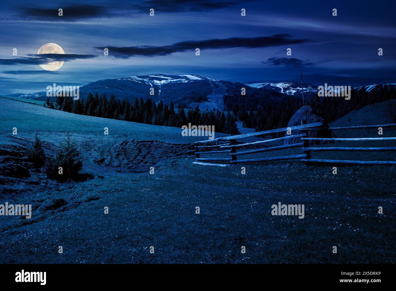 wooden fence across the grassy rural field at night. mountainous ...