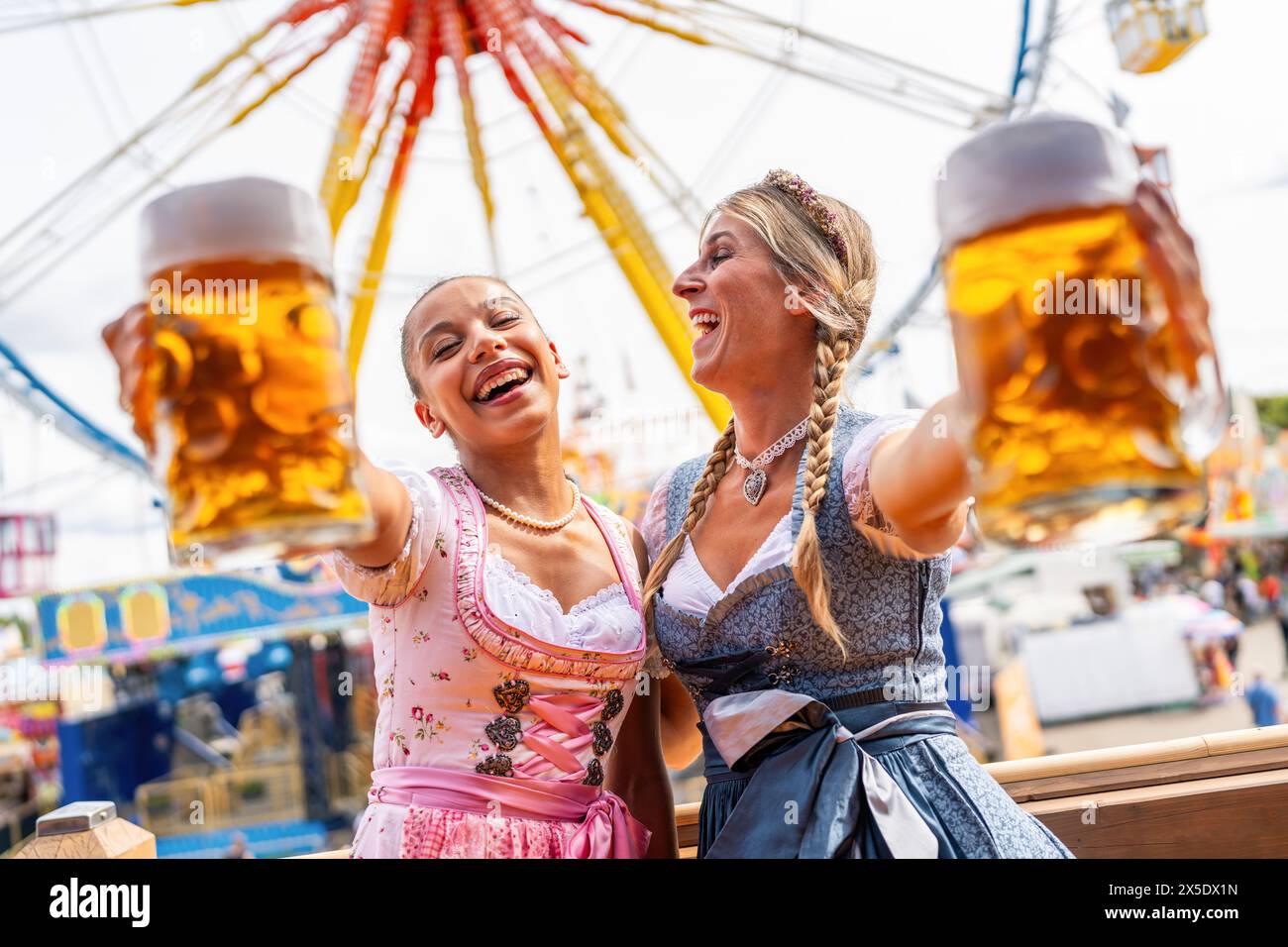 Two women in vibrant Bavarian dresses tracht joyfully toasting with ...