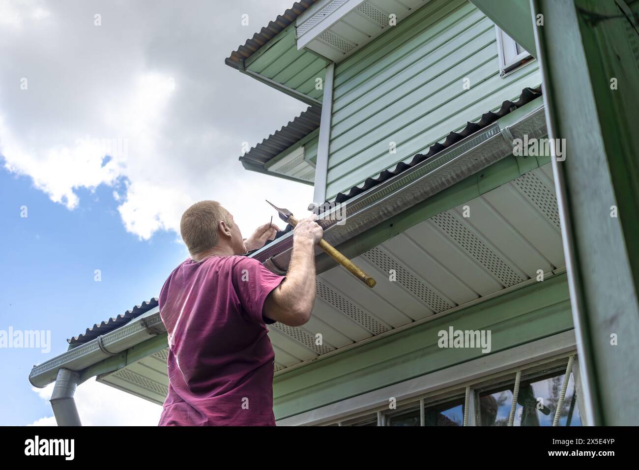 Adult man, owner of dacha with nail and an axe replacing hammer ...
