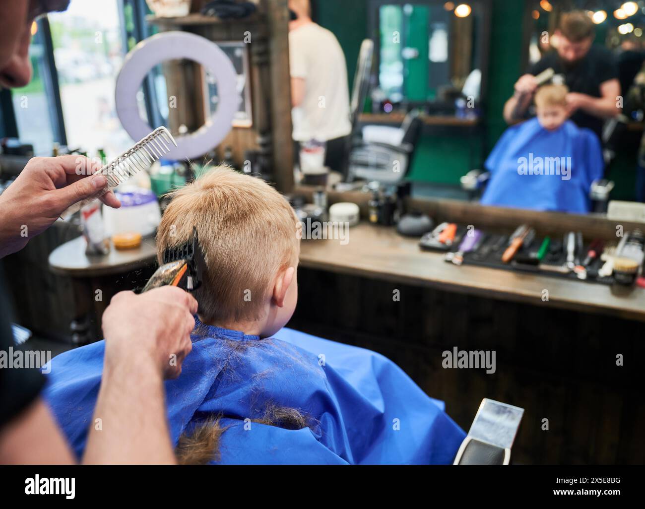 Hairdresser using electric shaver to cut boy's hair. Little kid getting ...