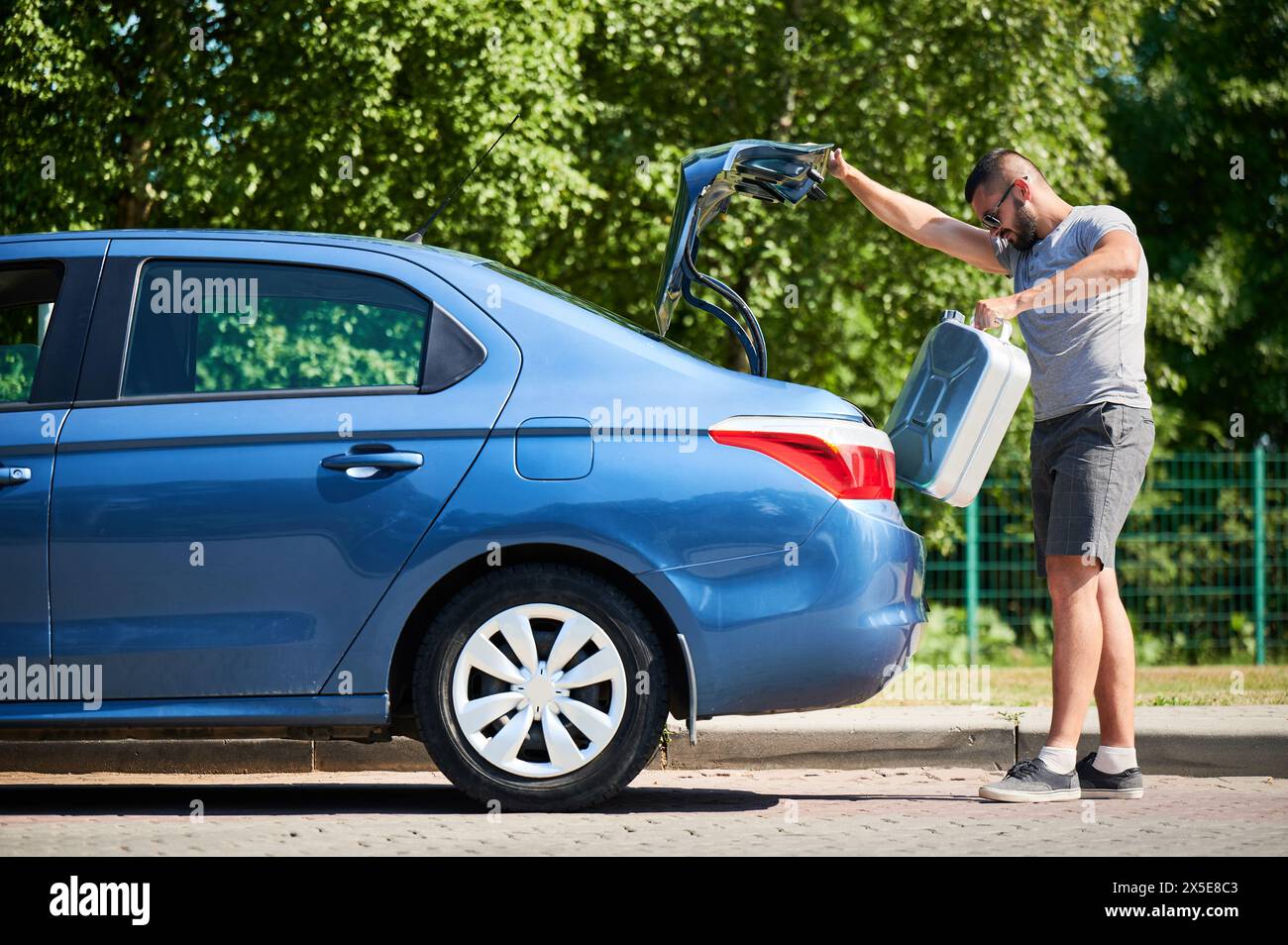 Young man taking out canister with gasoline from car trunk. Man glad ...