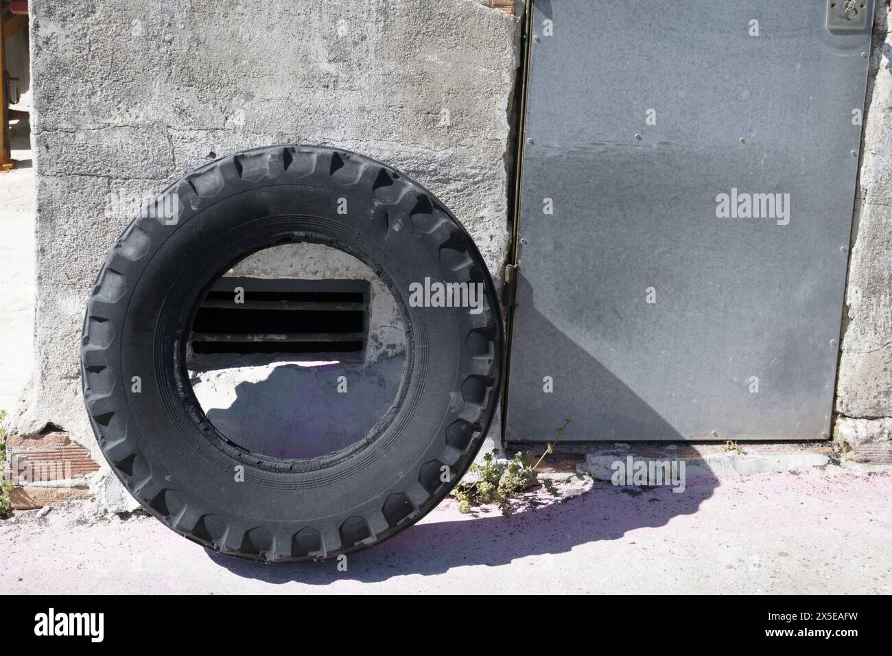 An old rubber wheel leaning on a wall with a metal door Stock Photo - Alamy