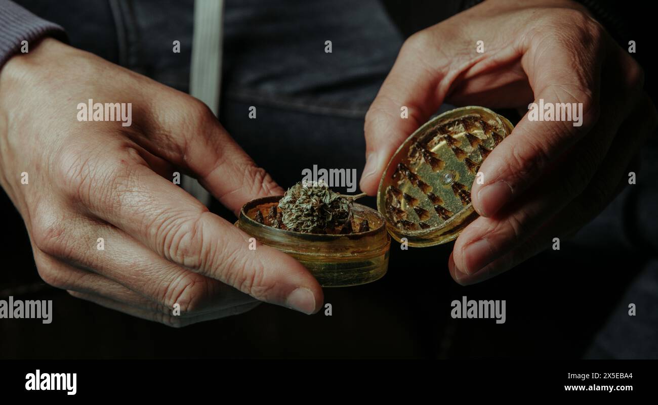 closeup of a man about to grind a cannabis bud with a used yellow ...
