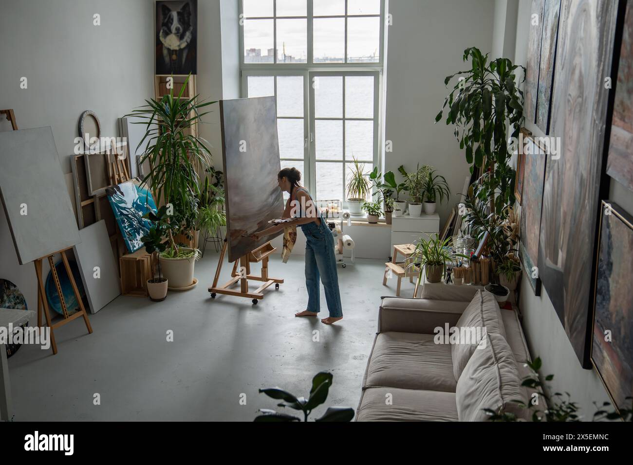 Modern woman artist creating artworks masterpieces at well-lit bright home creative art studio ...