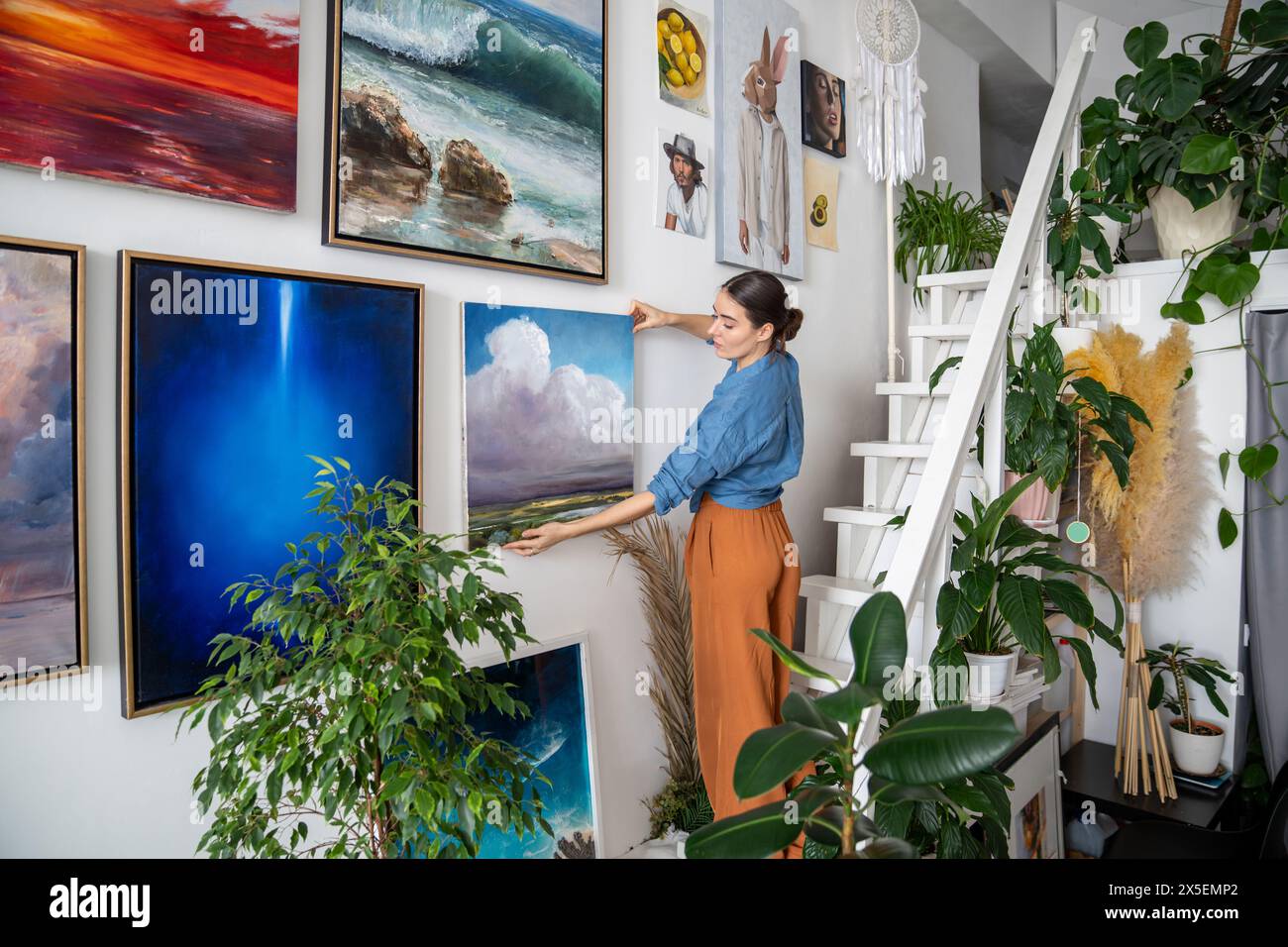 Focused woman artist hanging paintings on wall in creative art home ...