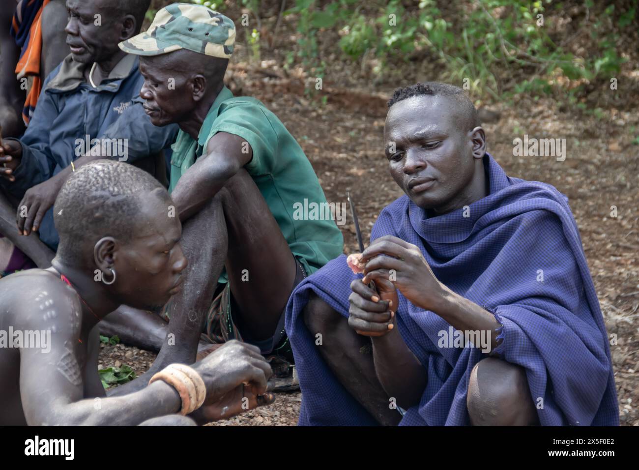 Mursi Tribe (Ethiopia) gathered around fire place, preparing, sharing ...