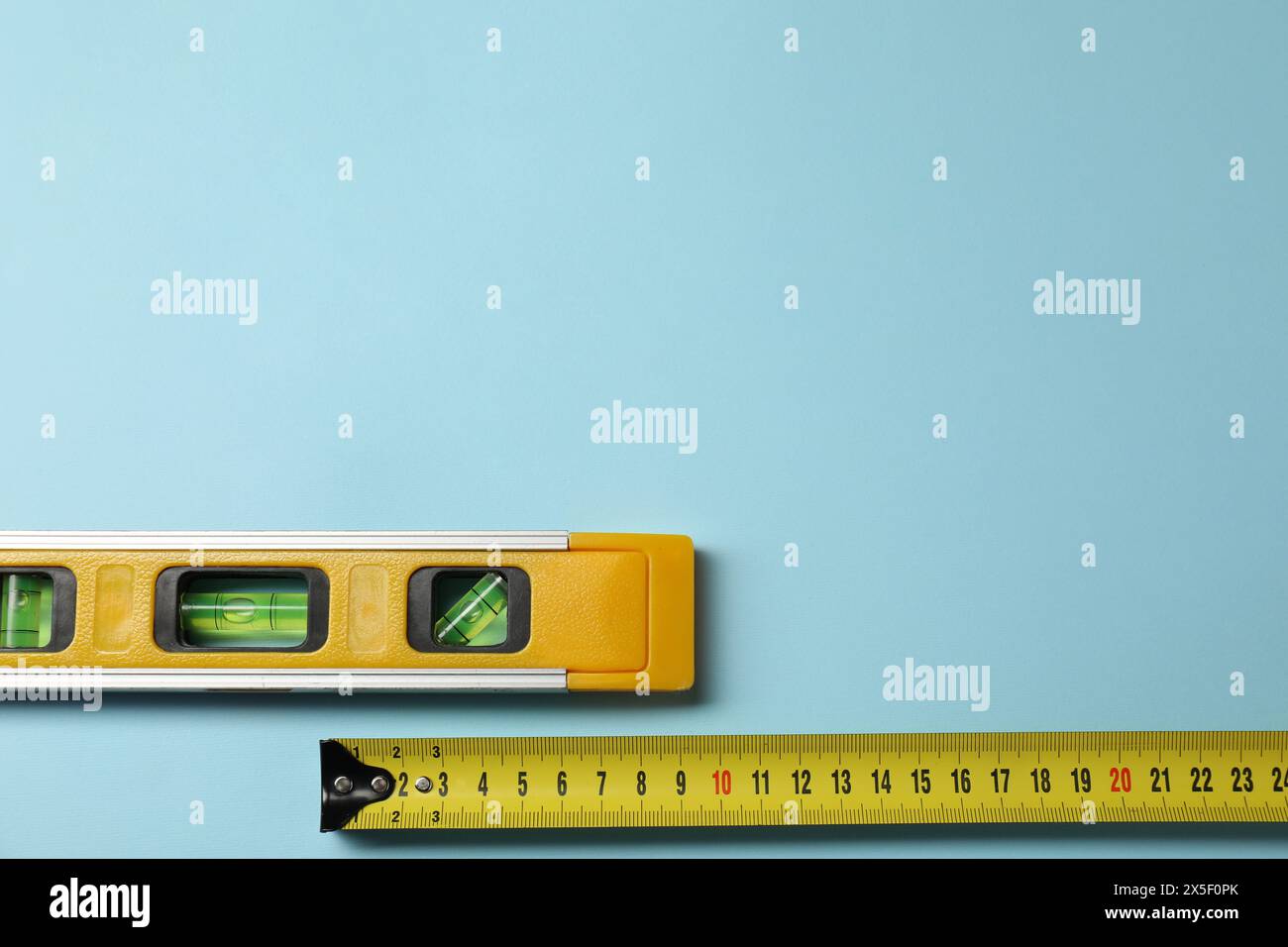 Building level and tape measure on light blue background, top view ...