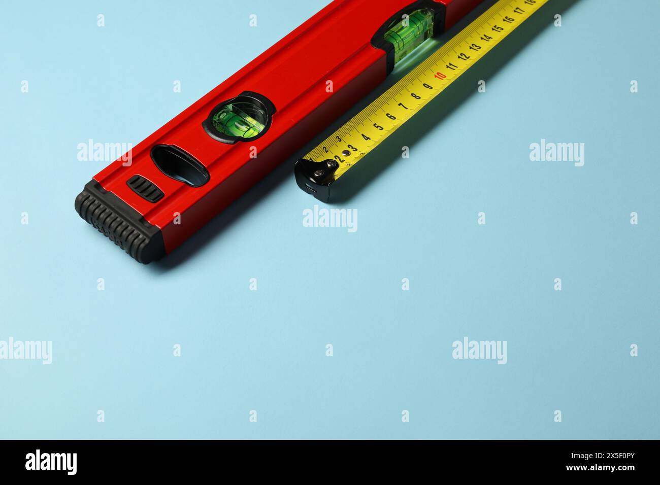 Building level and tape measure on light blue background. Space for ...