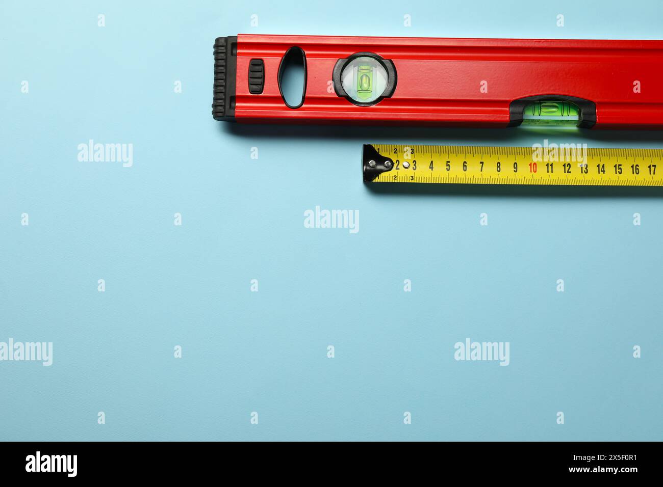 Building level and tape measure on light blue background, top view ...