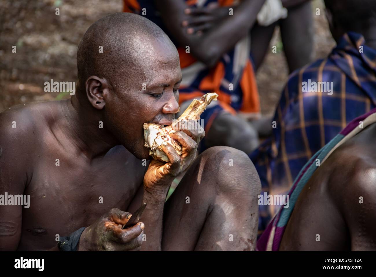 Members of Mursi Tribe in Ethiopia, in Omo valley, gathered around fire ...