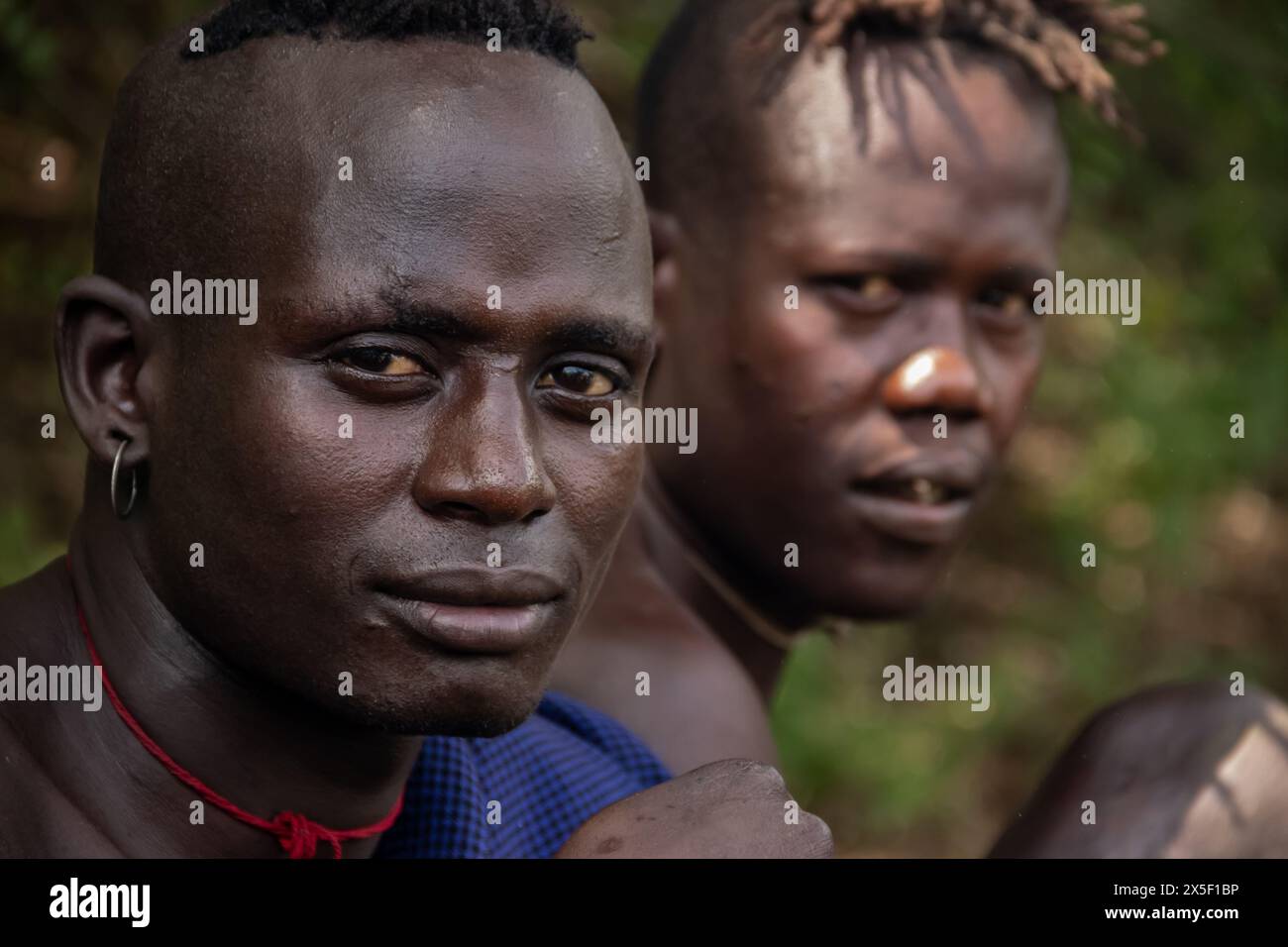 Members of Mursi Tribe in Ethiopia, in Omo valley, gathered around fire, eating meat from animal ...
