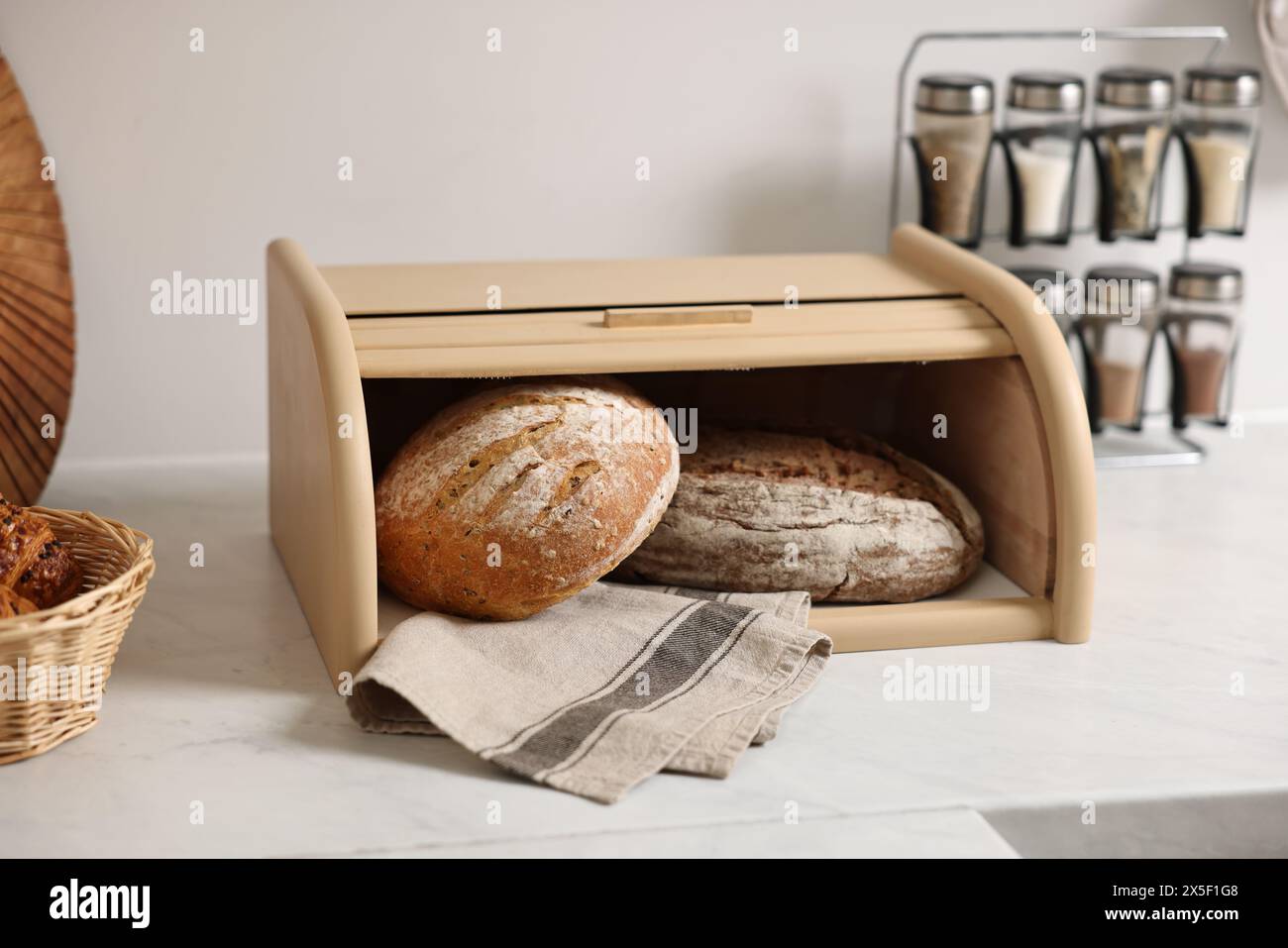 Wooden bread basket with freshly baked loaves on white marble table in ...