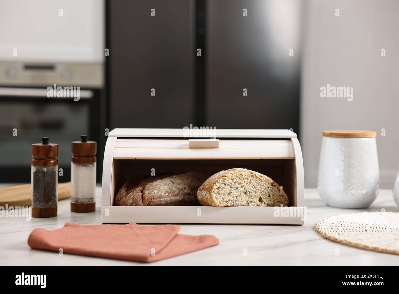 Wooden bread basket with freshly baked loaves on white marble table in ...