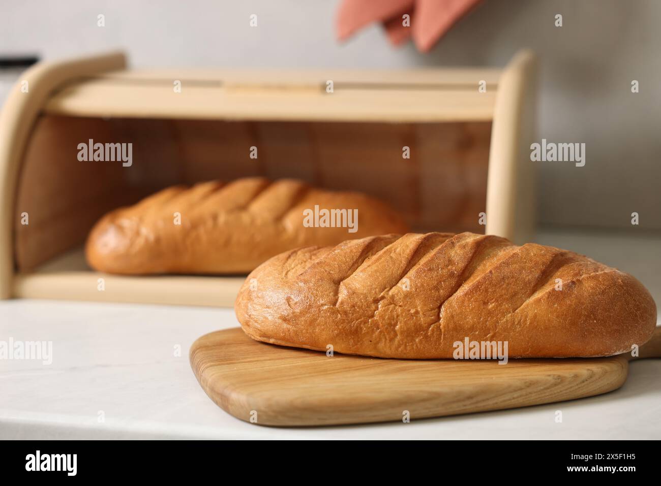 Wooden bread basket with freshly baked loaves on white marble table in ...