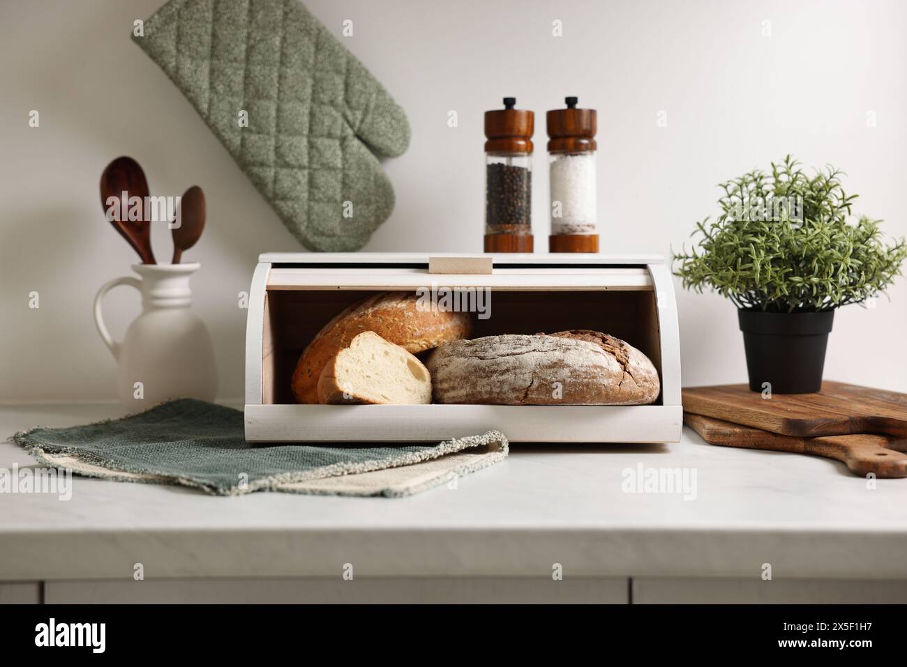 Wooden bread basket with freshly baked loaves on white marble table in ...