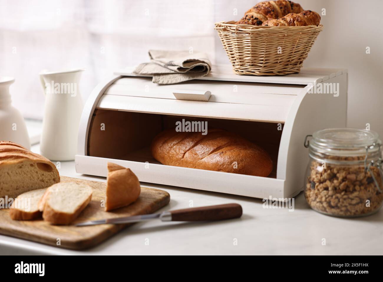 Wooden bread basket with freshly baked loaves on white marble table in ...