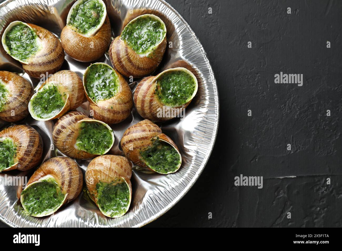 Delicious cooked snails on dark textured table, top view. Space for ...