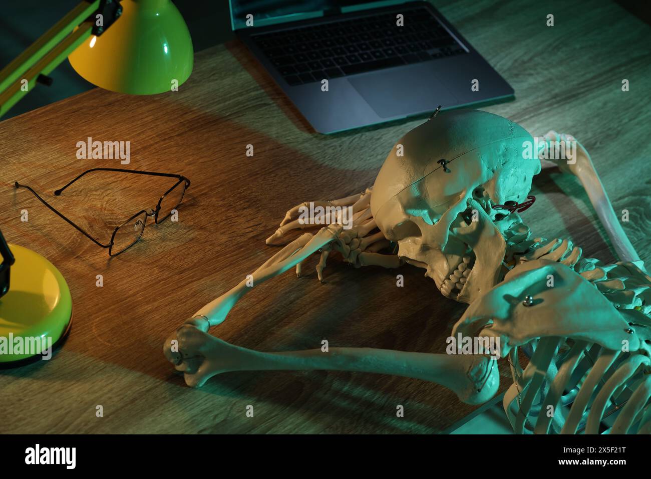 Waiting concept. Human skeleton sleeping at wooden table with laptop ...