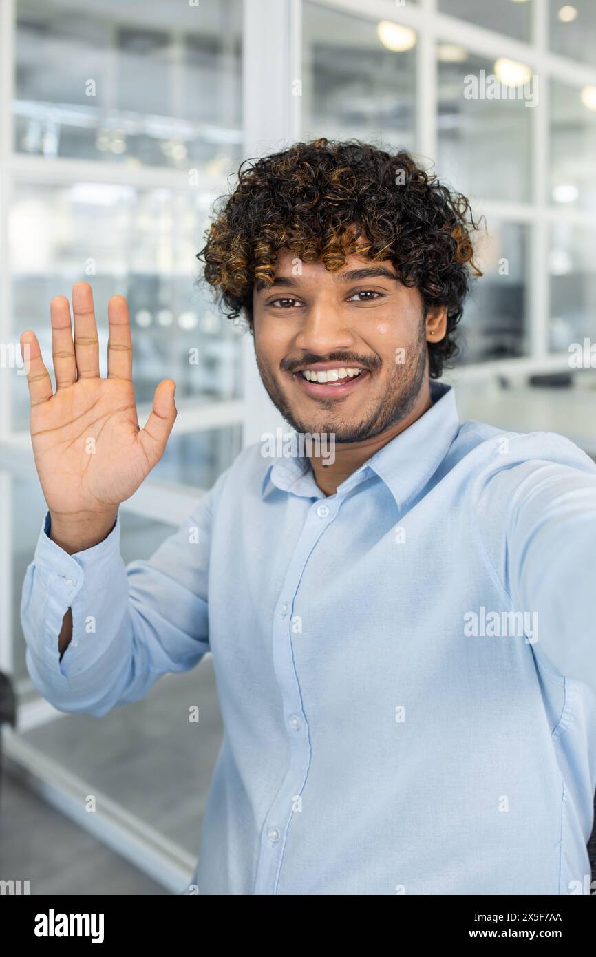 Cheerful young adult male with curly hair waving at the camera ...