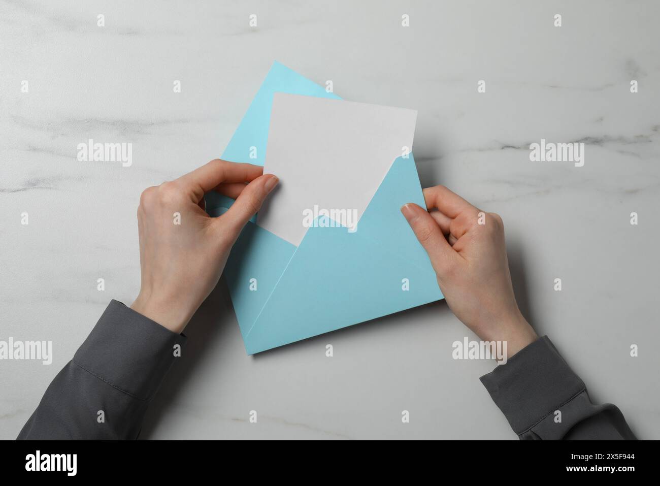 Woman taking card out of letter envelope at marble table, top view ...