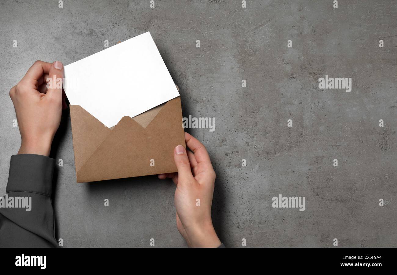 Woman taking card out of letter envelope at grey textured table, top ...