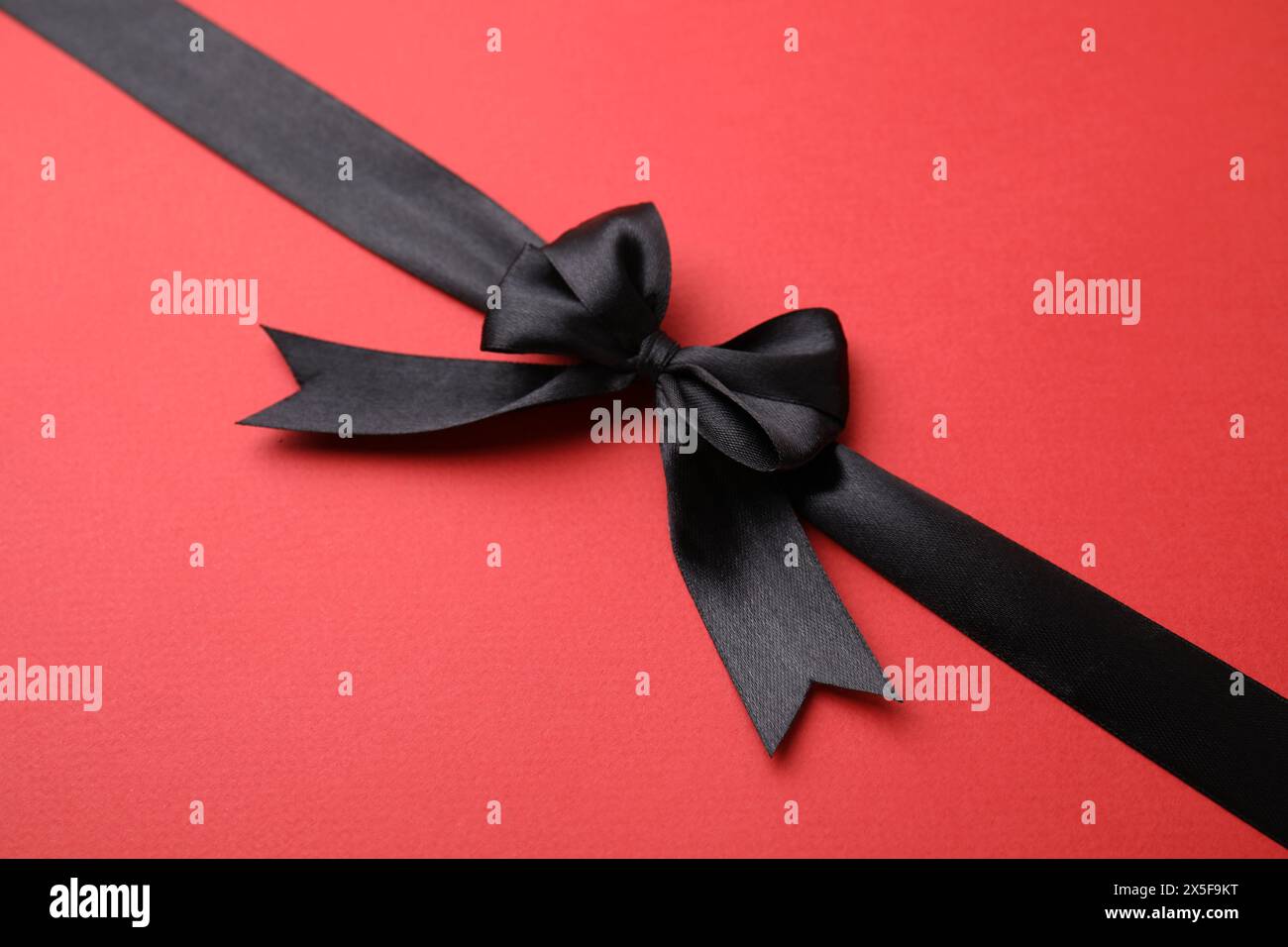 Black satin ribbon with bow on red background Stock Photo - Alamy