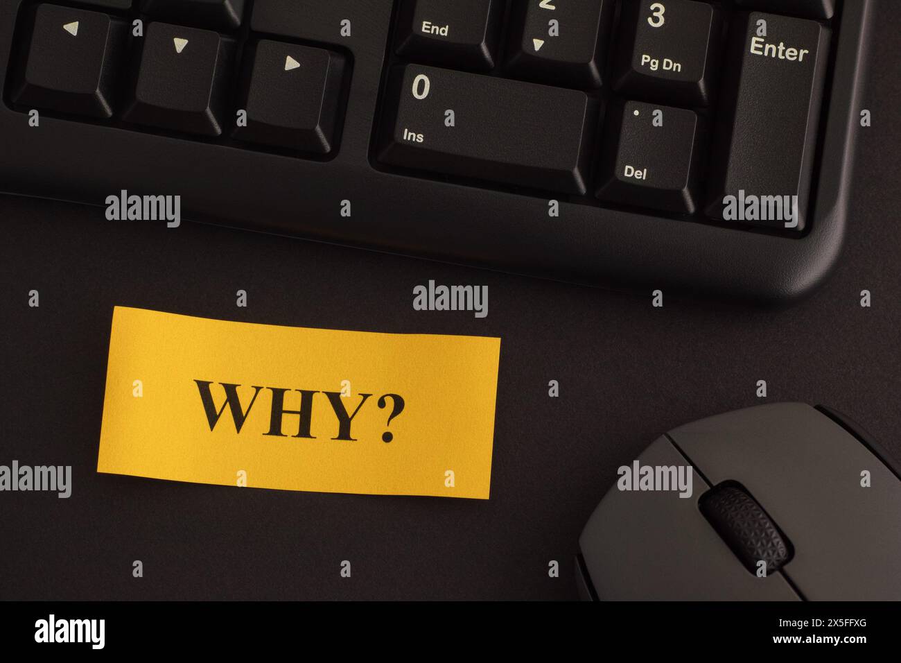 Paper note with writing Why? on a desk with black keyboard and grey ...