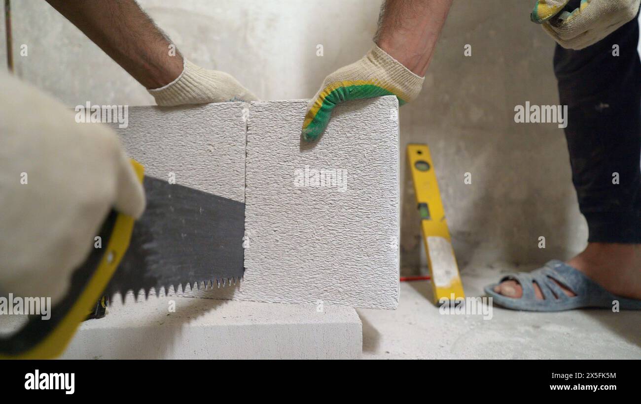 Close-up. A construction worker saws an aerated concrete block with a ...
