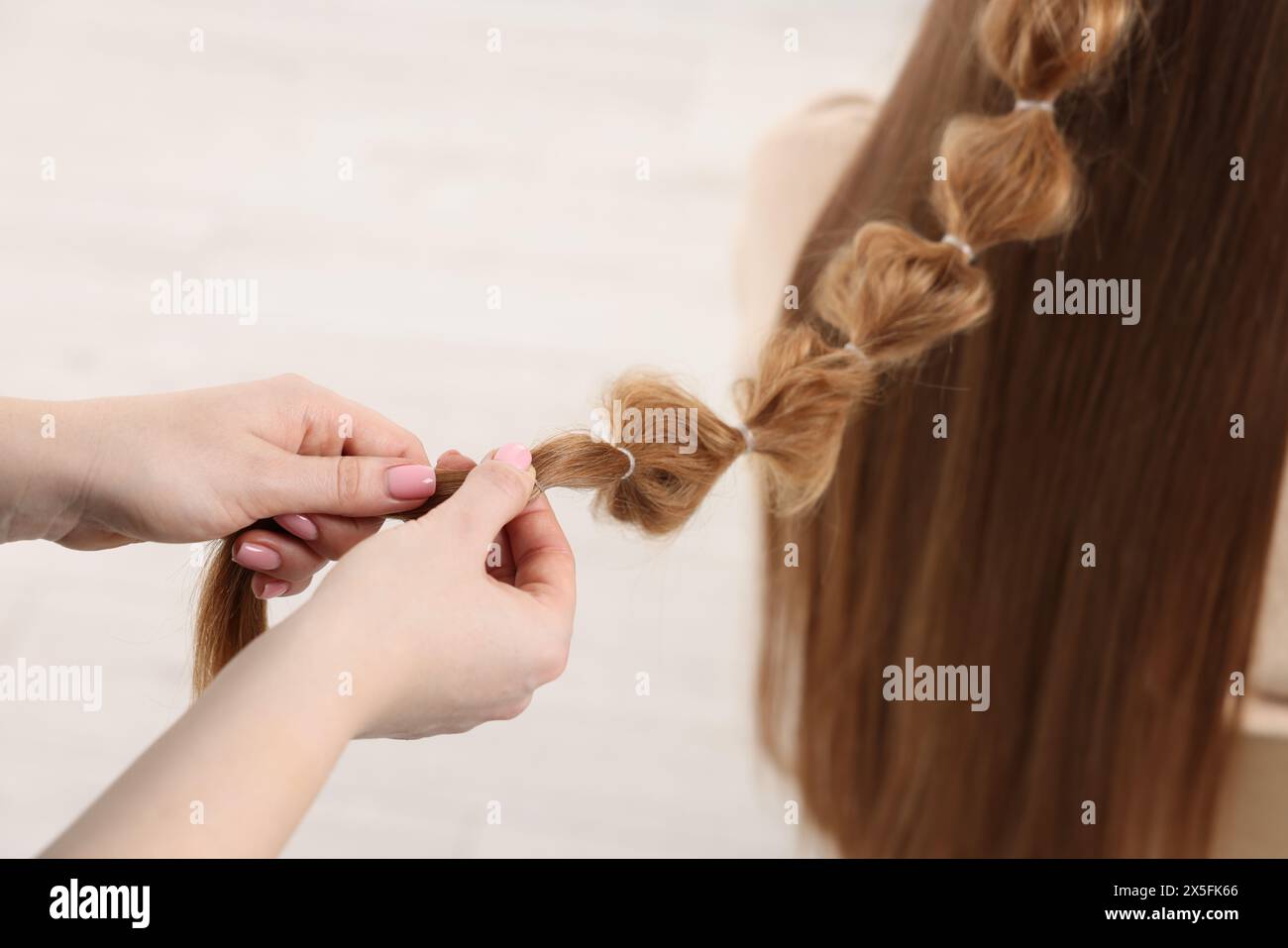 Professional stylist braiding woman's hair on blurred background ...