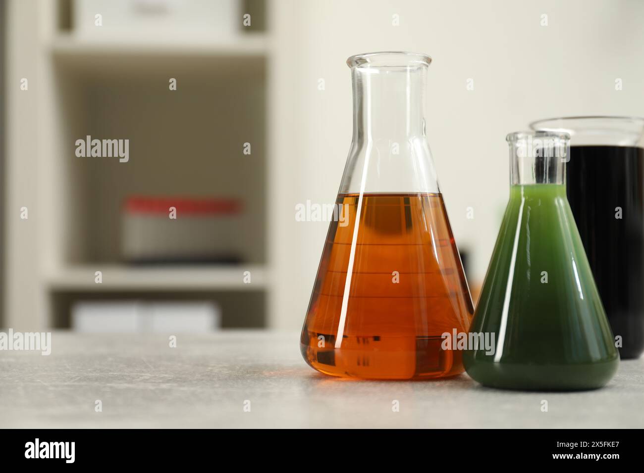 Flasks and beaker with different types of crude oil on light grey table ...