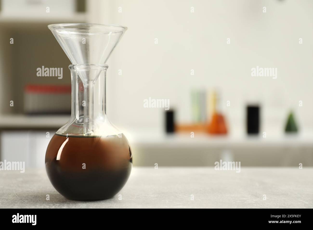 Flask with brown crude oil and filter funnel on light grey table, space ...