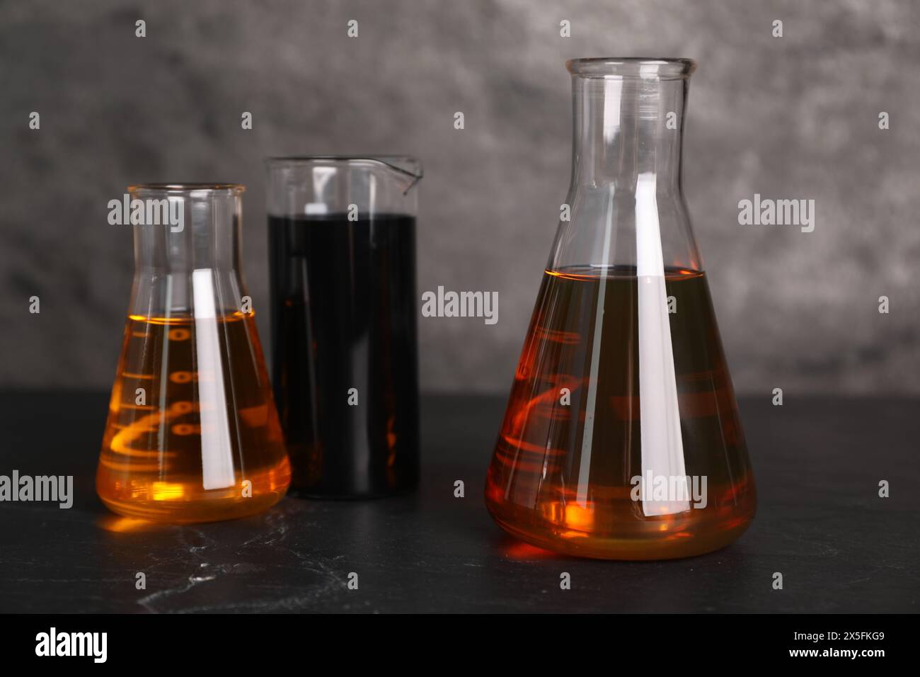Beaker and flasks with different types of oil on grey textured table ...