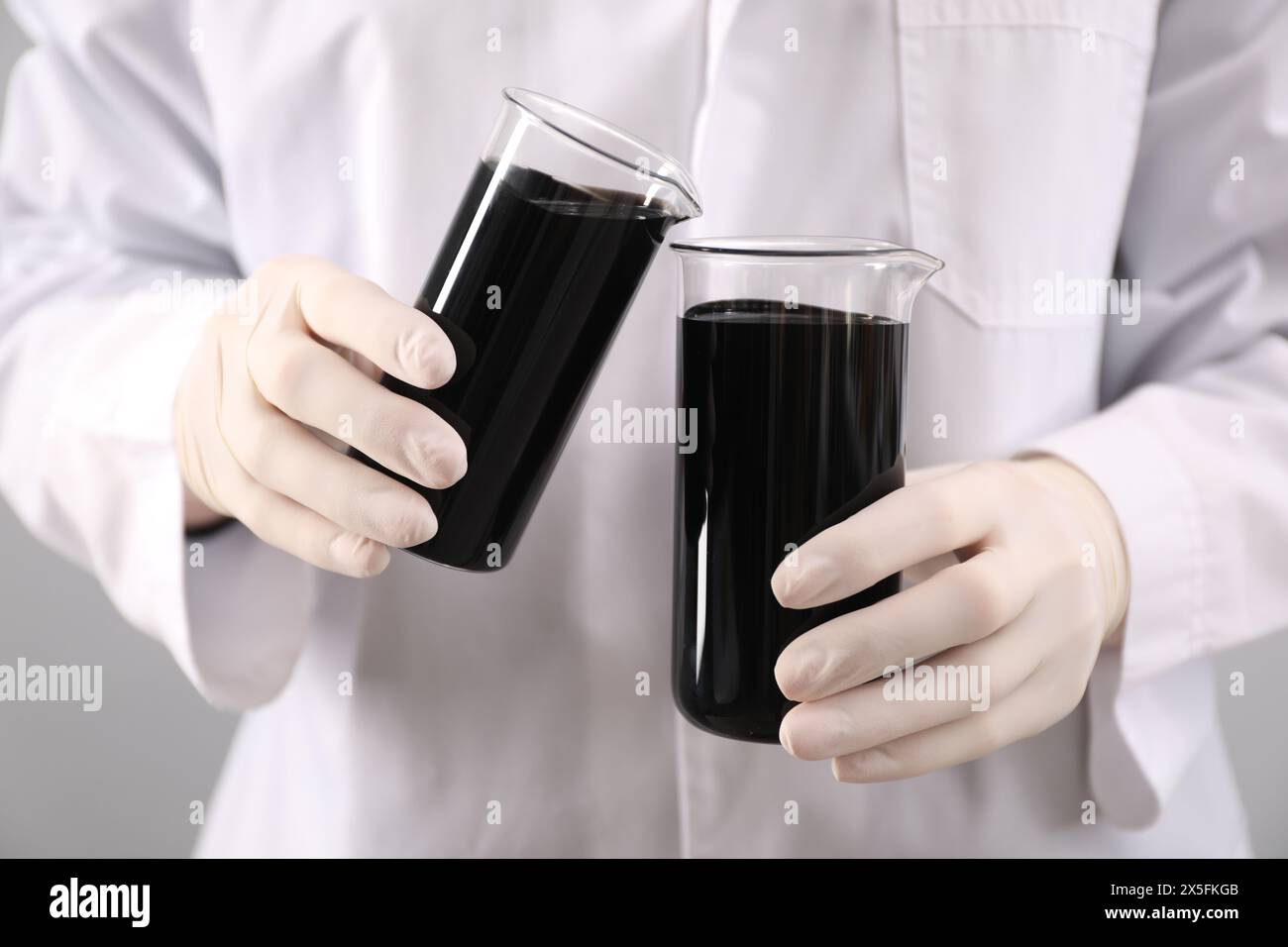 Woman pouring black crude oil into beaker on light background, closeup ...
