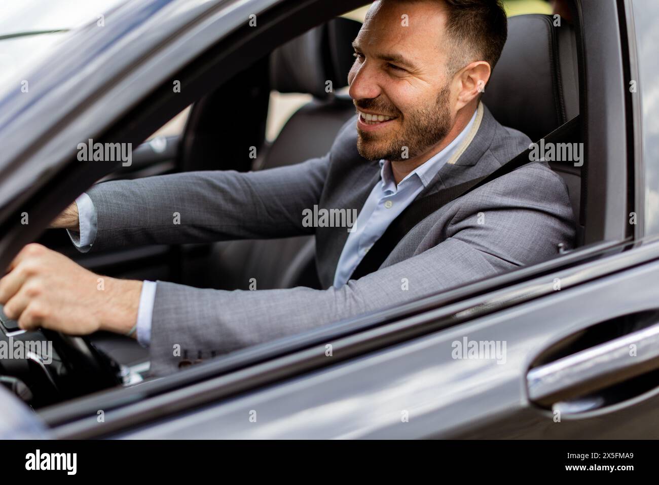 Joyful driver smiles while holding the wheel, cruising down the road in ...