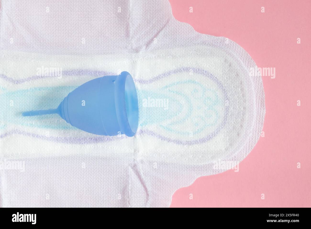 Blue menstrual cup is placed on sanitary pad, depicted against ...